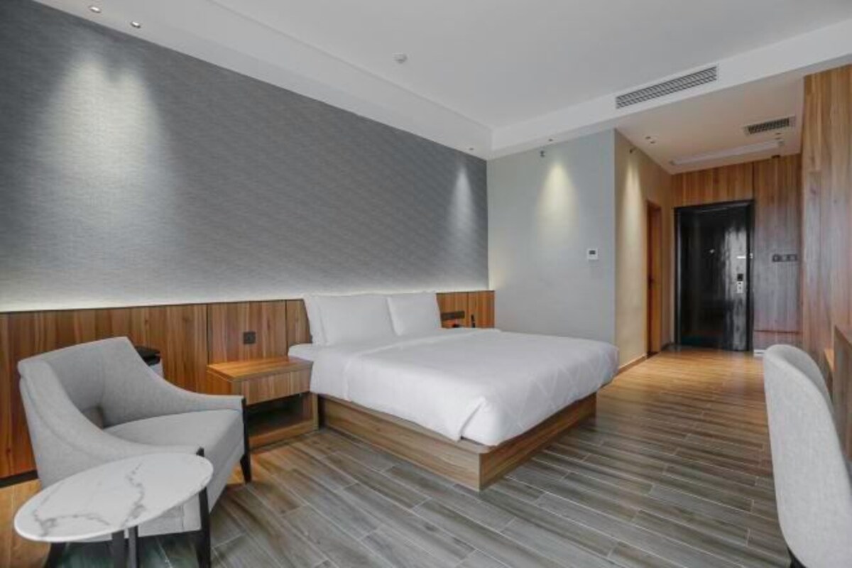 Quarto de hotel moderno com cama, uma cadeira, uma mesinha e piso de madeira.