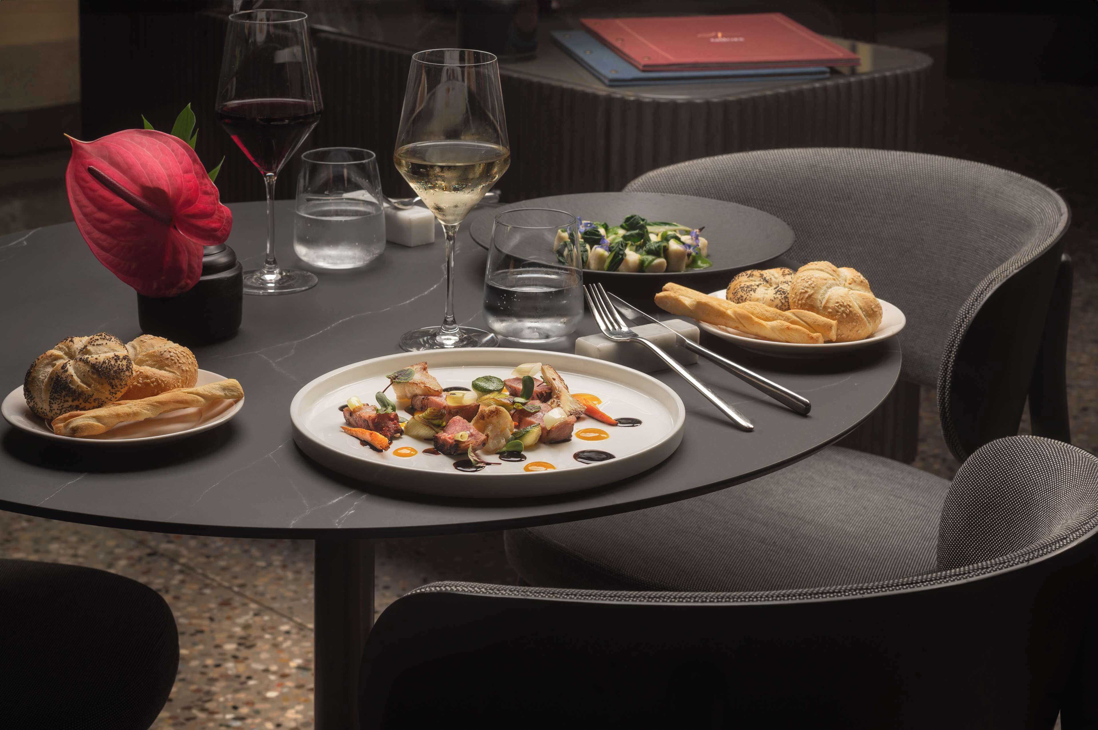 Uma mesa de jantar com pratos de comida, copos de vinho e talheres.