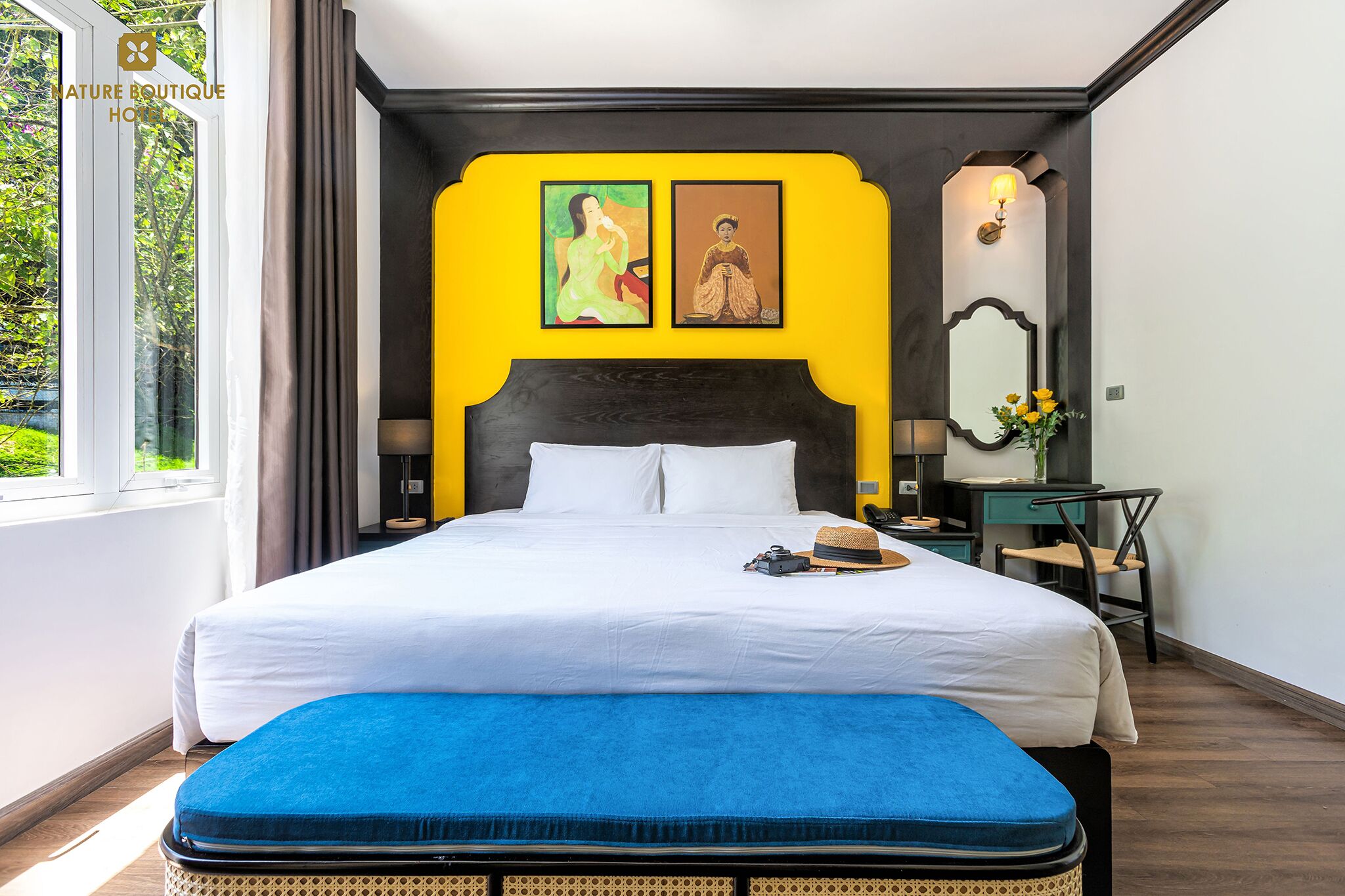 Quarto de hotel com uma cama grande, uma mesa de cabeceira com abajur, uma cadeira e uma janela com cortinas.