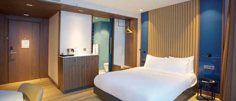 Quarto de hotel moderno com uma cama grande, um guarda-roupa de madeira, uma escrivaninha com cadeira e uma mesa redonda pequena.