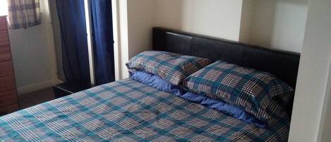 Quarto com cama, cabeceira e janela com cortinas.