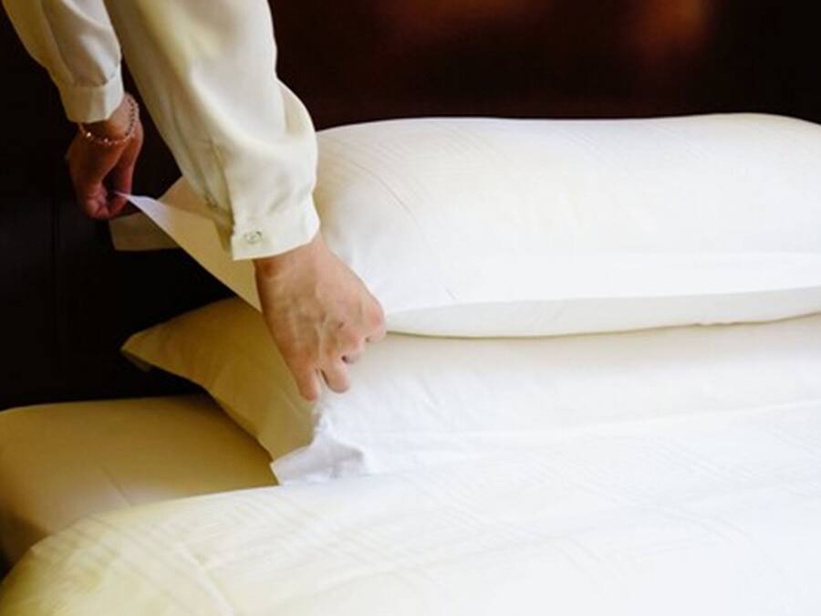 Mão ajustando um travesseiro branco na cama.