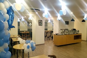 Quarto com piso de madeira, mesas, cadeiras e um espaço para buffet com recipientes de vidro.