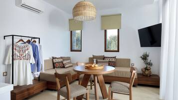 Uma sala de estar moderna com uma mesa de madeira redonda, dois sofás, uma TV fixada na parede e um cabideiro com roupas penduradas.