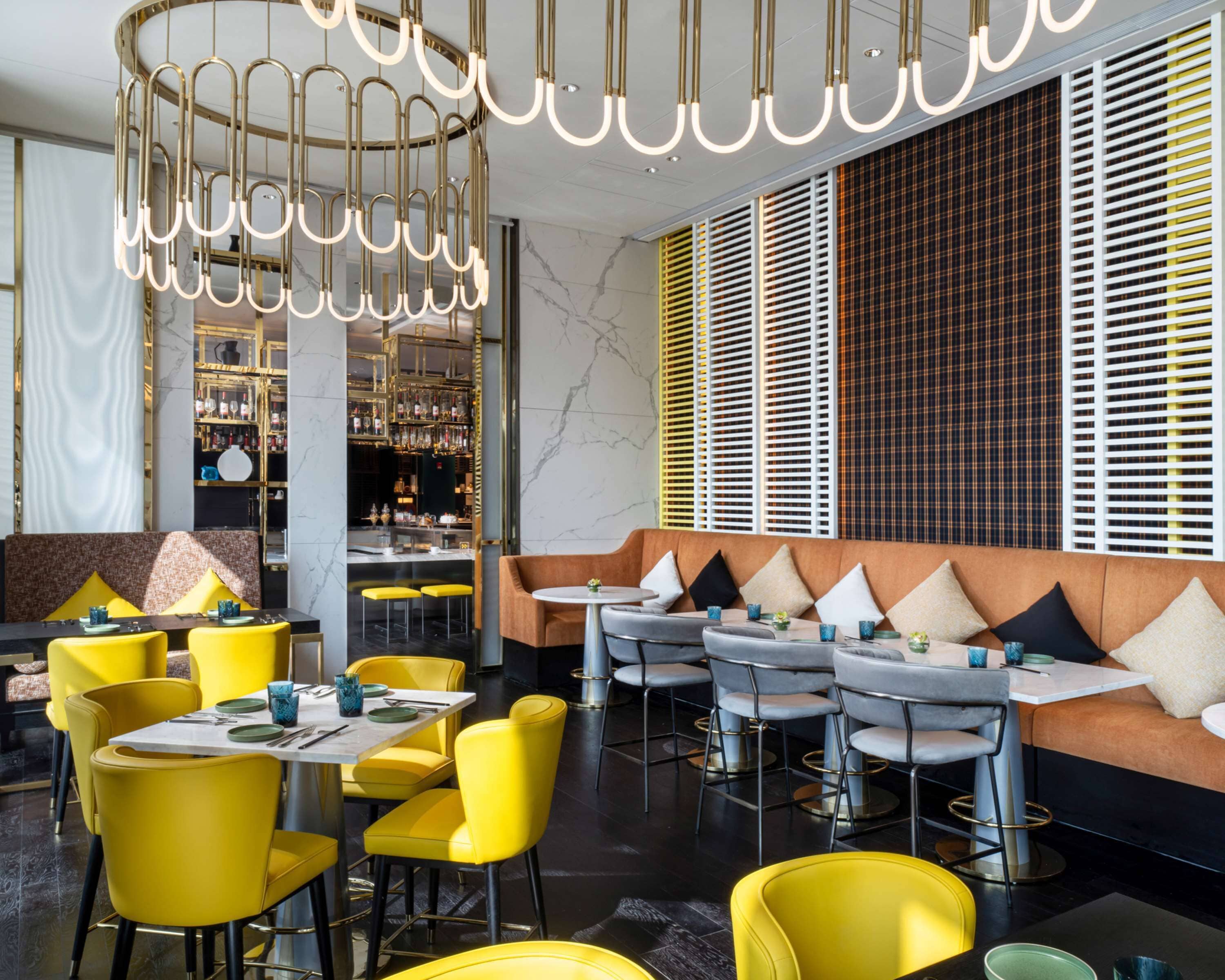 Interior moderno de restaurante com cadeiras amarelas, área de bar e espaço de estar com sofá e mesas.
