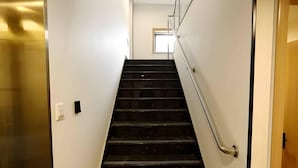 Uma escadaria com degraus pretos e corrimão, levando a uma porta no topo.