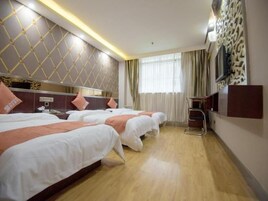 Quarto de hotel com três camas, televisão, escrivaninha e janela com cortinas.