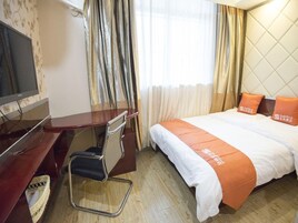 Quarto de hotel com cama, escrivaninha, cadeira, televisão e cortinas.