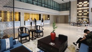 Um hall amplo com balcão de recepção, área de estar e um grande arranjo de plantas.