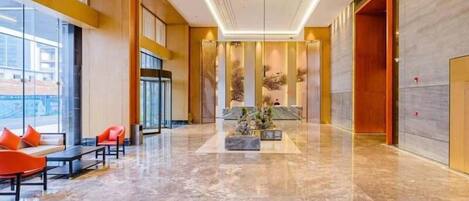 Um lobby moderno com piso de mármore, área de estar com cadeiras laranja e balcão de recepção.
