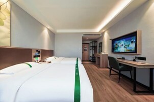 Quarto de hotel com uma cama grande, uma mesa, uma televisão e um banheiro visível através de uma porta aberta.