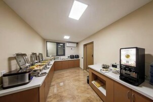 Cozinha com estações de buffet, máquina de café e televisão.