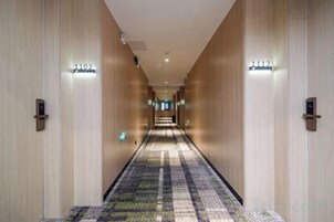 Corredor de hotel com piso em carpete, paredes de madeira e portas numeradas.