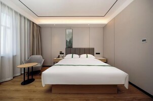 Quarto de hotel moderno com uma cama grande, uma mesa de cabeceira, uma cadeira e uma pequena mesa.
