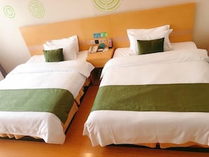 Quarto de hotel com duas camas, cada uma com roupa de cama branca e verde, cabeceira de madeira e mesa de cabeceira com telefone e uma pequena mesa.