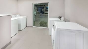 Uma lavanderia equipada com duas máquinas de lavar e uma secadora, porta de vidro que dá para área externa, e chão revestido com azulejos.