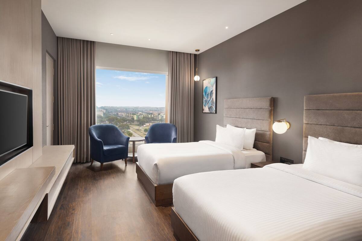 Quarto de hotel com duas camas, uma televisão, uma escrivaninha e uma cadeira.