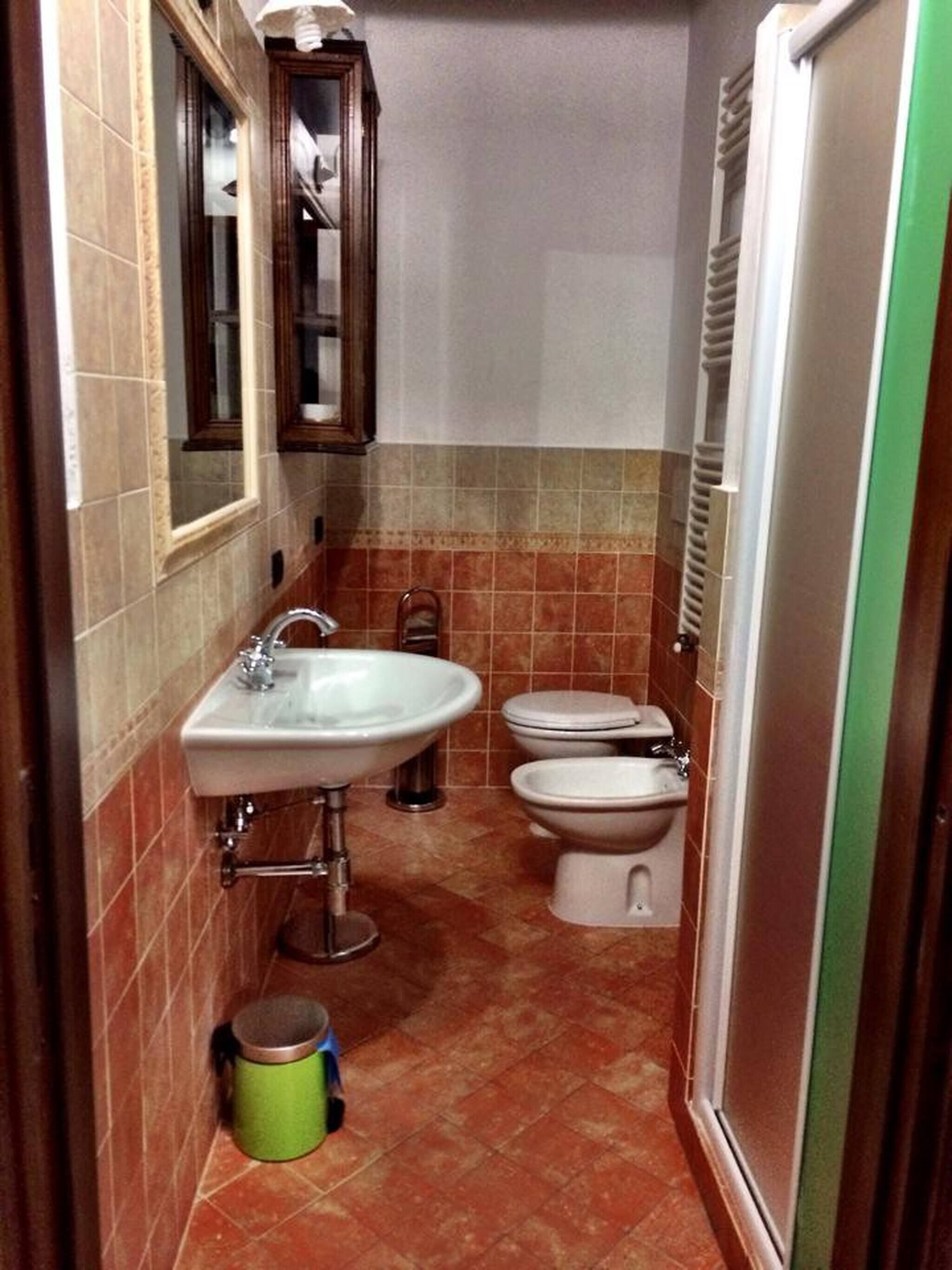 Casa de banho pequena com lavatório, duas sanitas e um cesto de lixo.