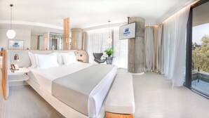 Quarto de hotel moderno com uma cama grande, uma escrivaninha, uma cadeira, uma televisão e vista para árvores e água.