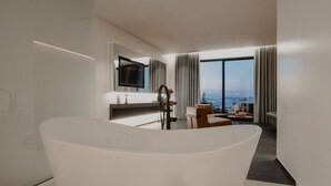 Quarto de hotel moderno com uma banheira grande, uma televisão de tela plana, área de jantar com vista e uma janela ampla.