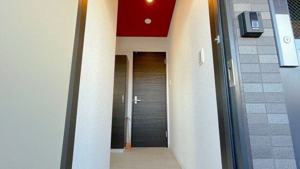 Um corredor moderno com teto vermelho, porta de vidro e parede texturizada.