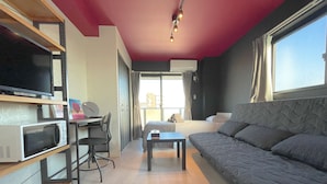 Quarto moderno com sofá, escrivaninha com cadeira, televisão e micro-ondas.