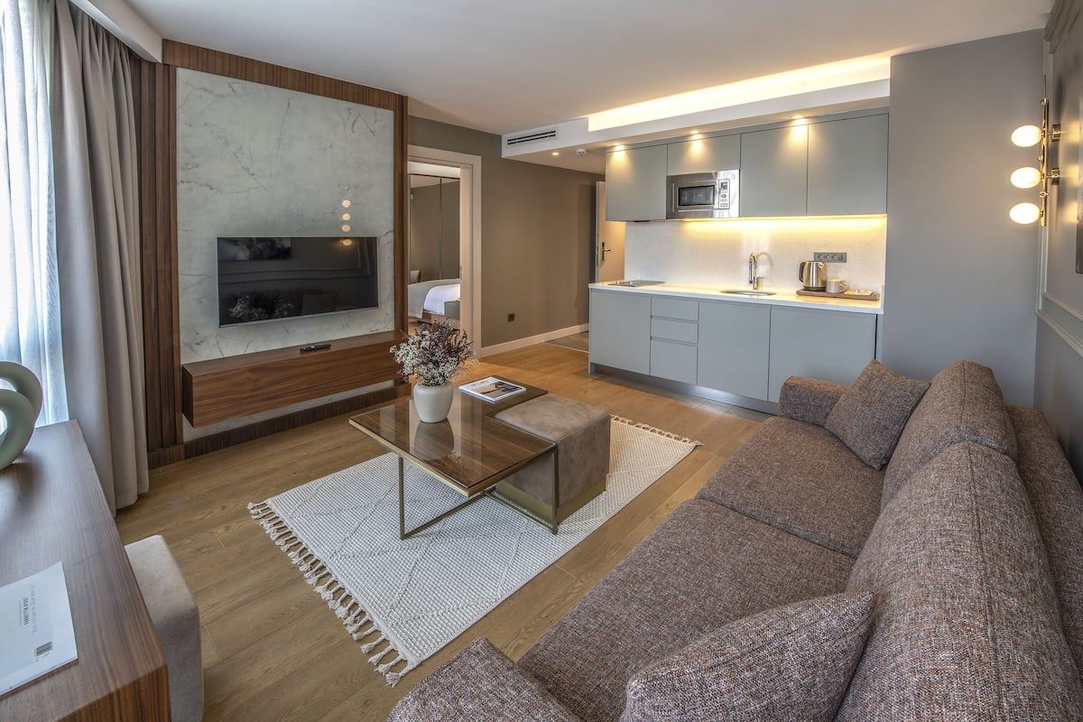 Uma sala de estar moderna com televisão de tela plana, um sofá, uma mesa de centro e uma área de cozinha com micro-ondas.