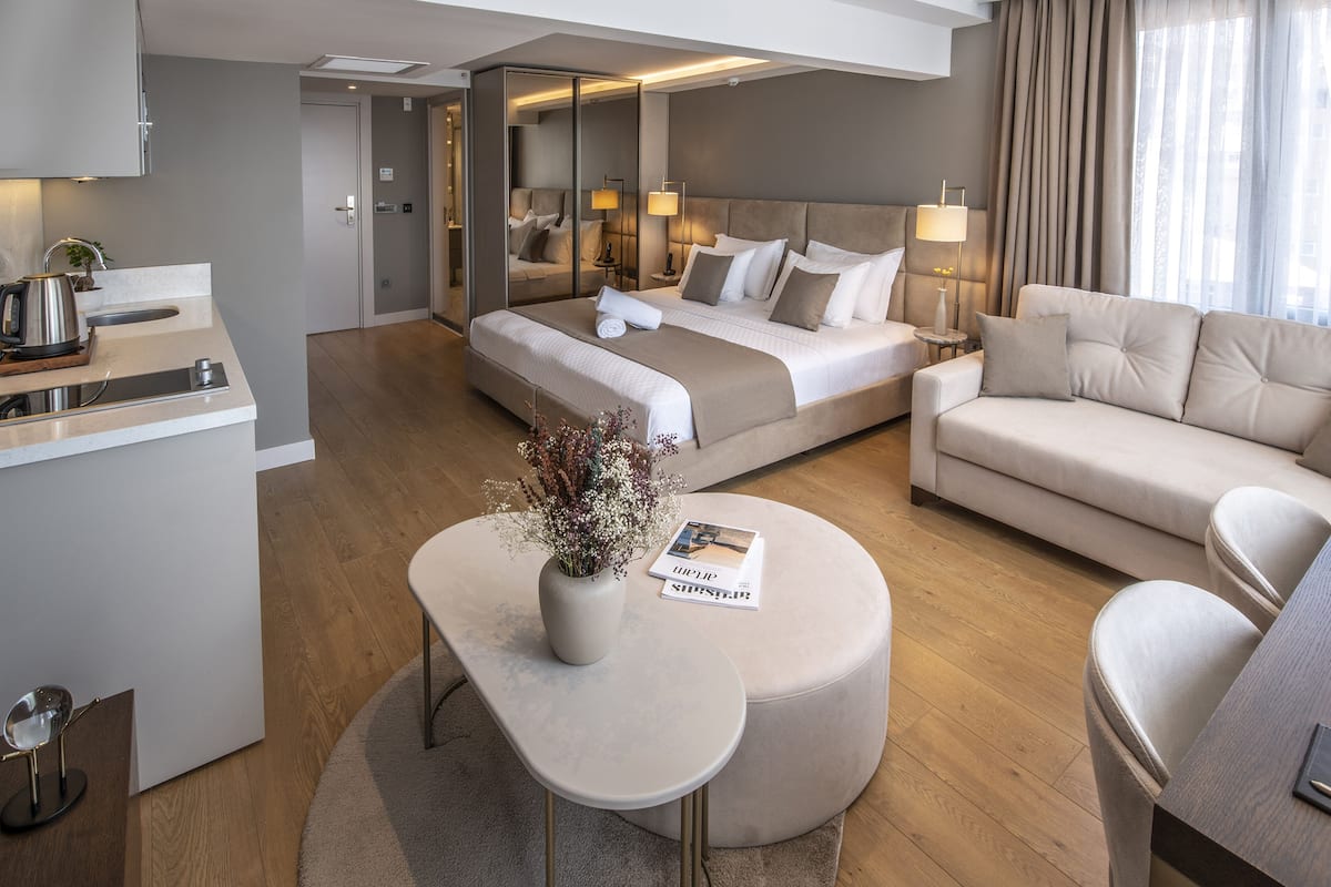 Quarto de hotel moderno com uma cama grande, um sofá, uma mesa pequena e uma cozinha.