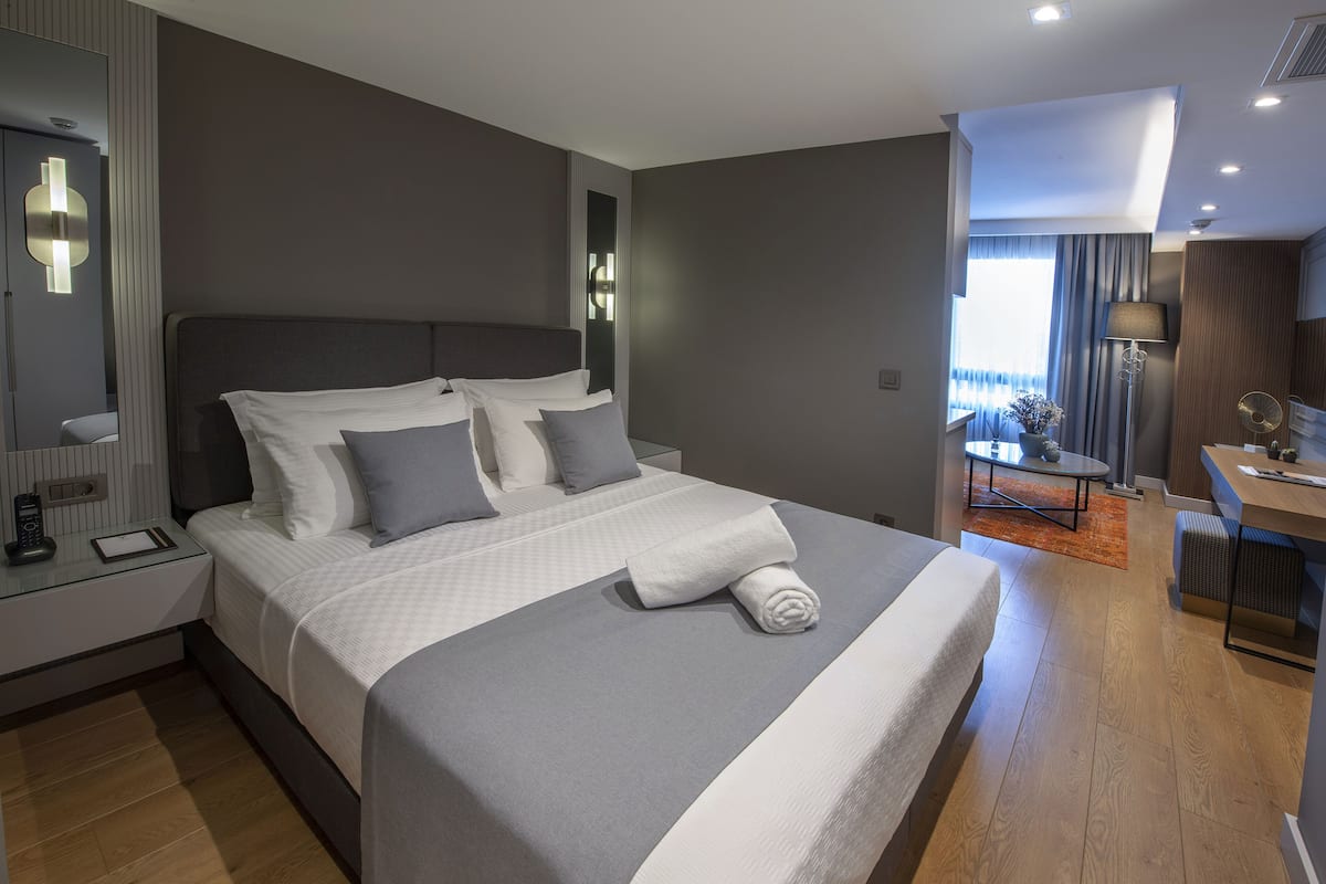 Quarto de hotel moderno com uma cama grande, mesas de cabeceira, uma escrivaninha e uma cadeira.