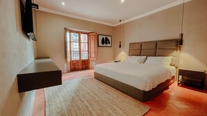 Um quarto com cama, mesas de cabeceira, televisão fixada na parede, porta com janela e tapete no chão.