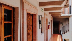Um corredor com portas e janelas de madeira, soalho em azulejos e varanda com grades.