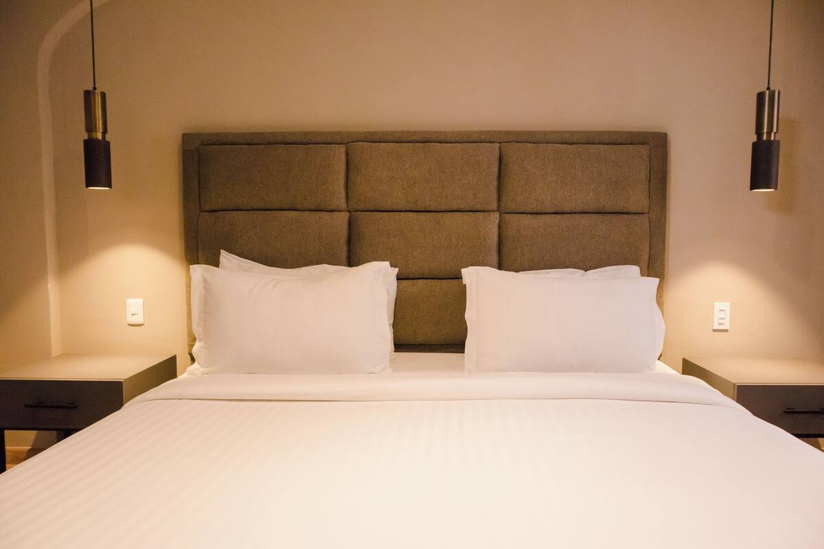 Quarto de hotel com uma cama grande, duas mesas de cabeceira e cabeceira acolchoada.
