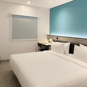 Quarto de hotel moderno com uma cama grande, uma escrivaninha com cadeira e um projetor fixado na parede.