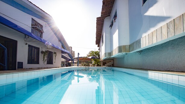 Piscina com azulejos azuis translúcidos, cercada por edifícios com paredes brancas e detalhes azuis.