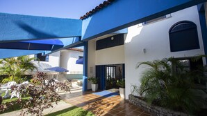 Um pátio com toldo azul, plantas em vasos e área de piso com azulejos.