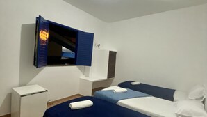 Quarto de hotel com duas camas, uma TV fixada na parede, uma mesinha e uma luminária no teto.