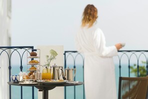Disposição de café da manhã com bandeja escalonada, um vaso com planta e uma pessoa vestindo um roupão branco.