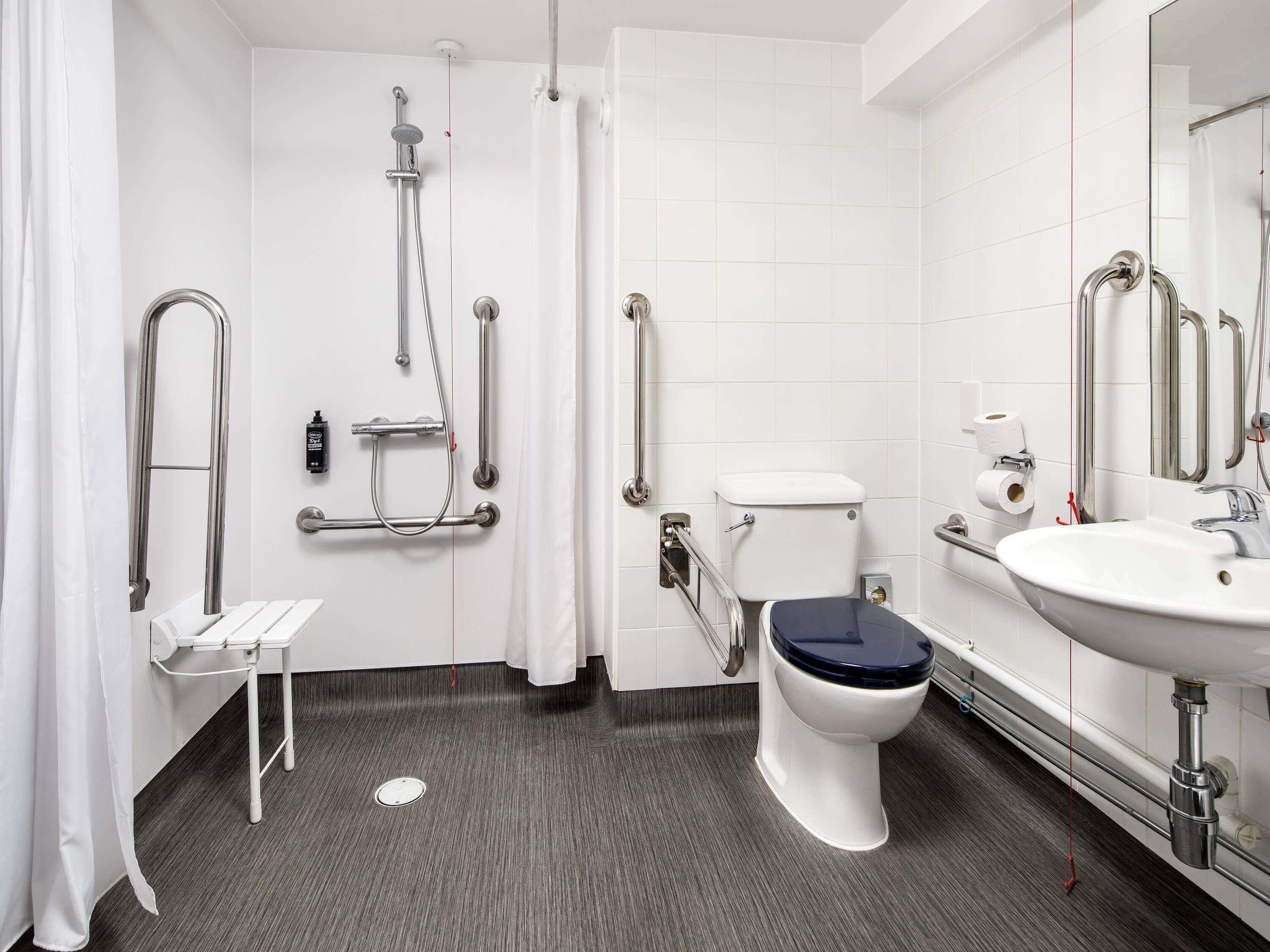 Casa de banho moderna com sanita, bidé e lavatório, equipada com barras de apoio e um banco de chuveiro.