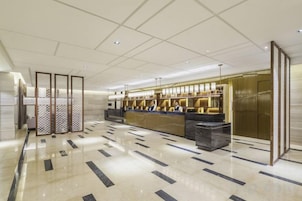 Um saguão de hotel com balcão de recepção, área de estar e piso estampado.