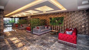 Um hall amplo com parede em padrão herringbone, um sofá cinza com detalhes vermelhos e um sofá vermelho com detalhes brancos.