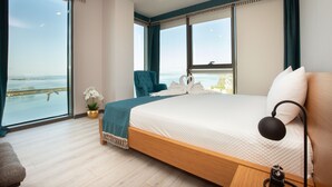 Quarto com cama grande, uma cadeira, uma escrivaninha e vista para o mar.