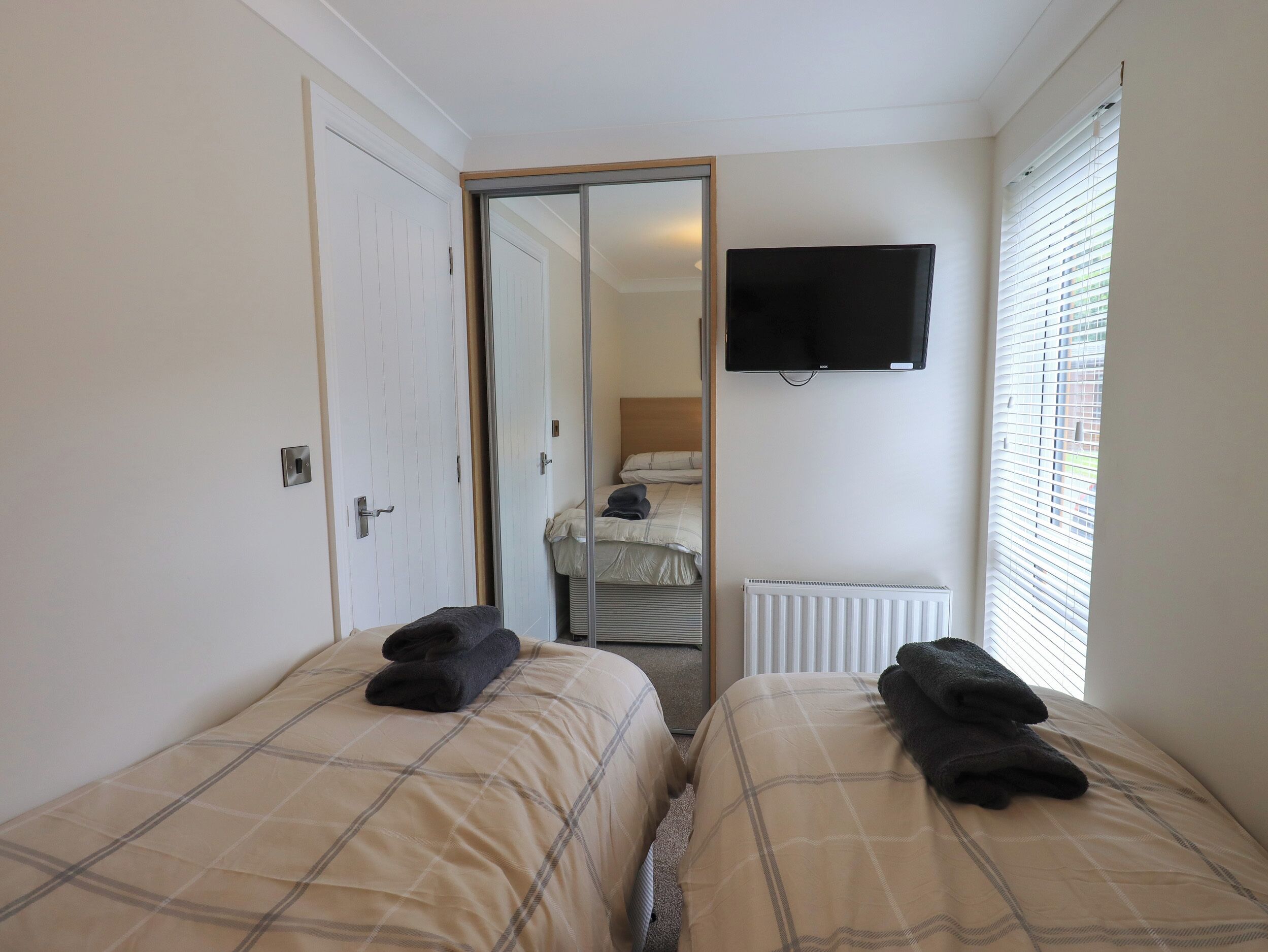 Quarto de hotel com duas camas, uma televisão presa à parede, um radiador e uma janela com persianas.