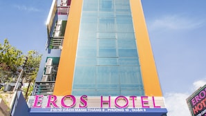 Exterior do Hotel Eros, com fachada moderna, entrada de vidro destacada e esquema de cores azul e amarelo.