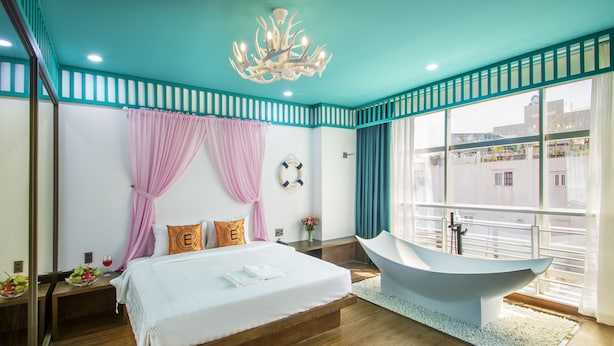 Quarto moderno com uma cama grande, uma banheira e vista para prédios através de grandes janelas.