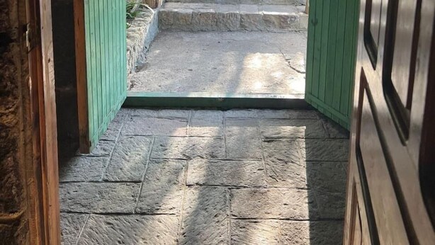 Estrutura de madeira com portas verdes que dão para um caminho de pedras.