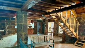 Um interior rústico com escada de madeira, pilares de pedra e um banco de madeira.