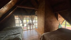 Quarto de sótão aconchegante com duas camas, uma mesa pequena e vista para o exterior através de grandes janelas.