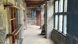 Um corredor com paredes de pedra, vigas de madeira, um portão de metal e uma janela com vista para o exterior.