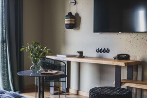 Uma sala de estar moderna com uma mesa redonda, uma cadeira preta, um pequeno vaso de plantas, um banco de madeira e uma televisão de tela plana na parede.