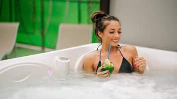 Uma pessoa em uma banheira de hidromassagem com uma bebida, em um ambiente esverdeado.